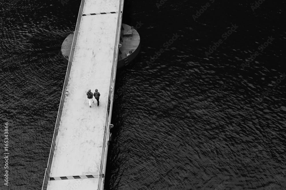 Two people walking on a floating bridge near the port of Geiranger in ...