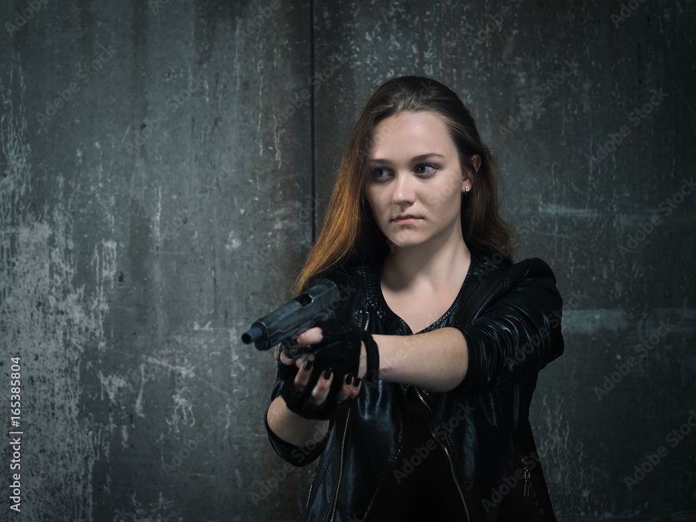 young girl in a black leather jacket with a gun. Luxurious long red ...