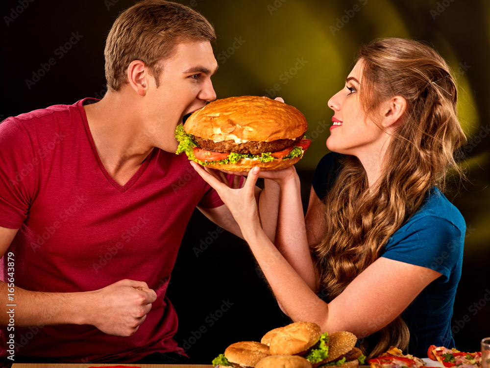Couple eating fast food. Man and woman treat big hamburger with ham ...
