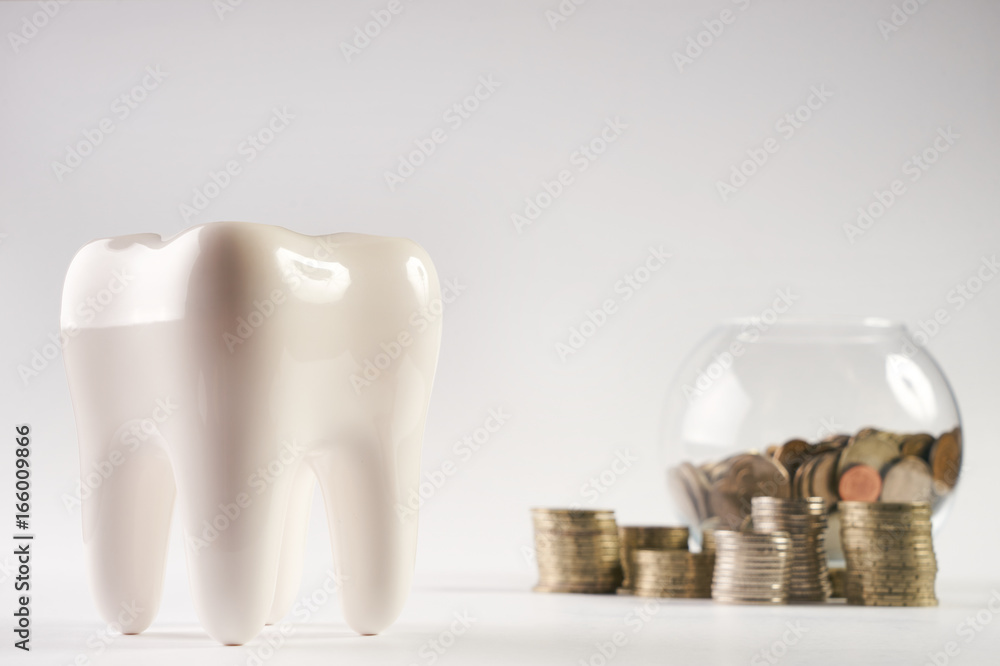 White healthy human enamel tooth model and glass piggy box with stacked ...