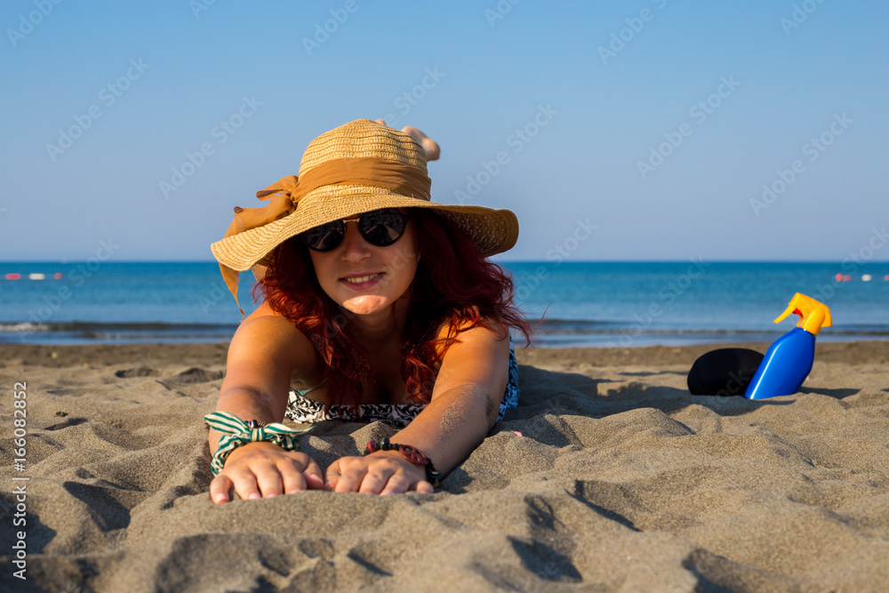 A young girl lying on the stomach on a beach in the sand, stretched out ...