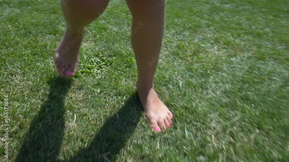 Children's barefoot legs walks on summer green grass. Bare feet of a ...