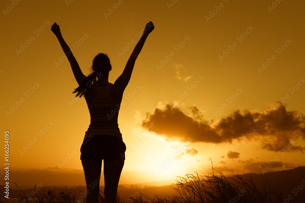 Happy victorious woman with her arms up facing the sunset. Stock Photo ...