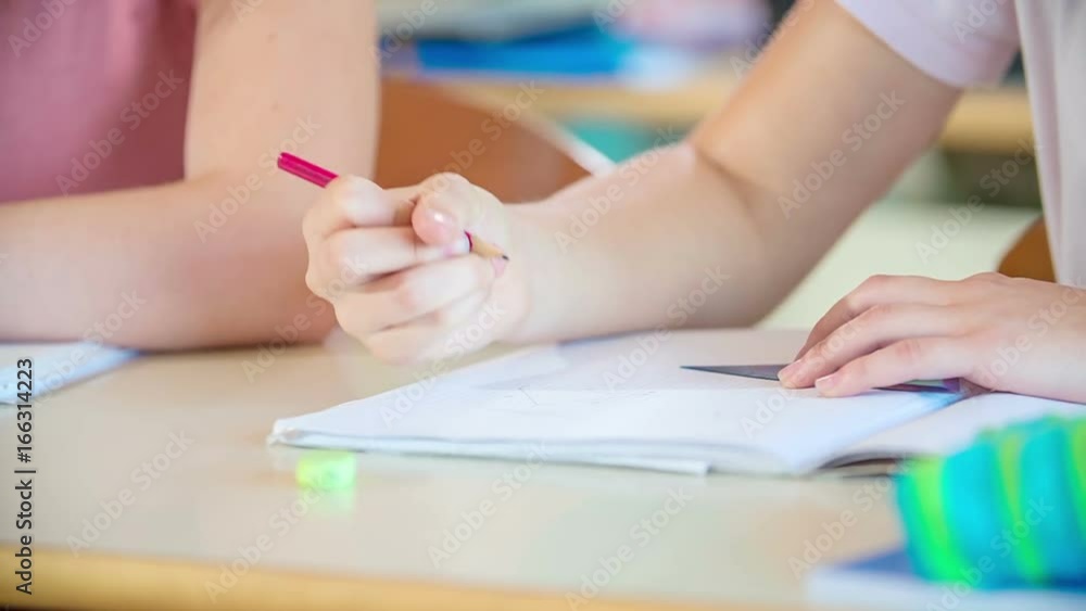 A young girl is writing something down into her notebook with a pencil ...