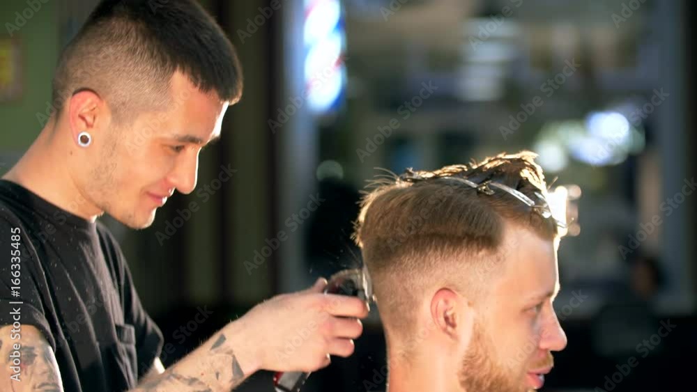 Professional tattooed barber giving a new haircut to his client in a ...