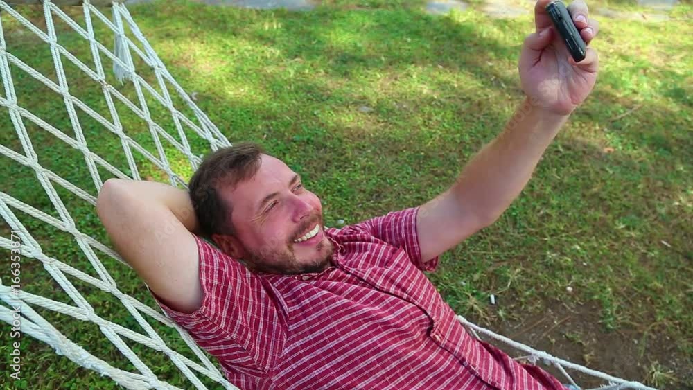 Adult handsome happy man wearing casual red shirt lying on hanging rope ...