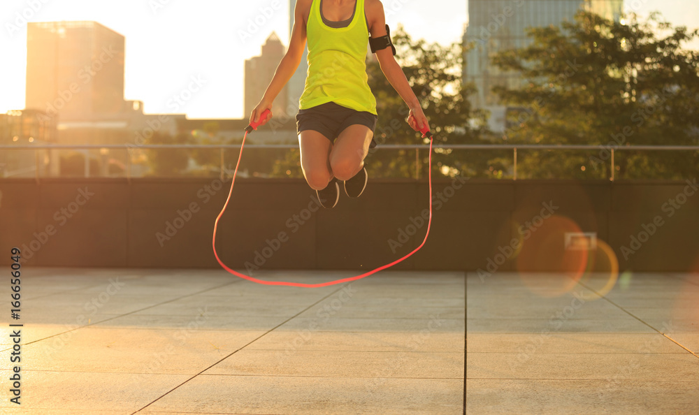 Young woman jumping rope at sunrise city building roof Stock Photo ...