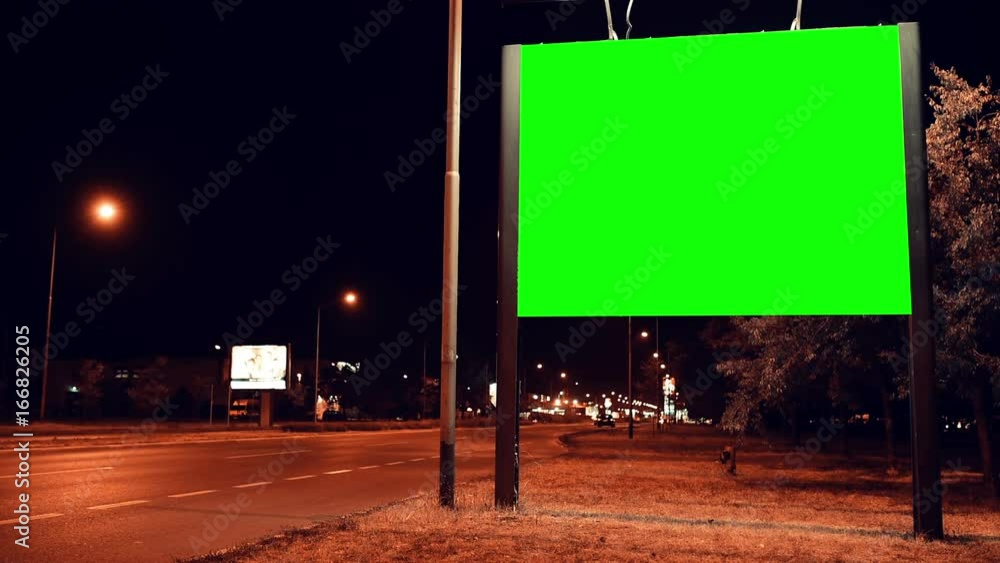 Blank green screen advertising billboard on street at night with ...