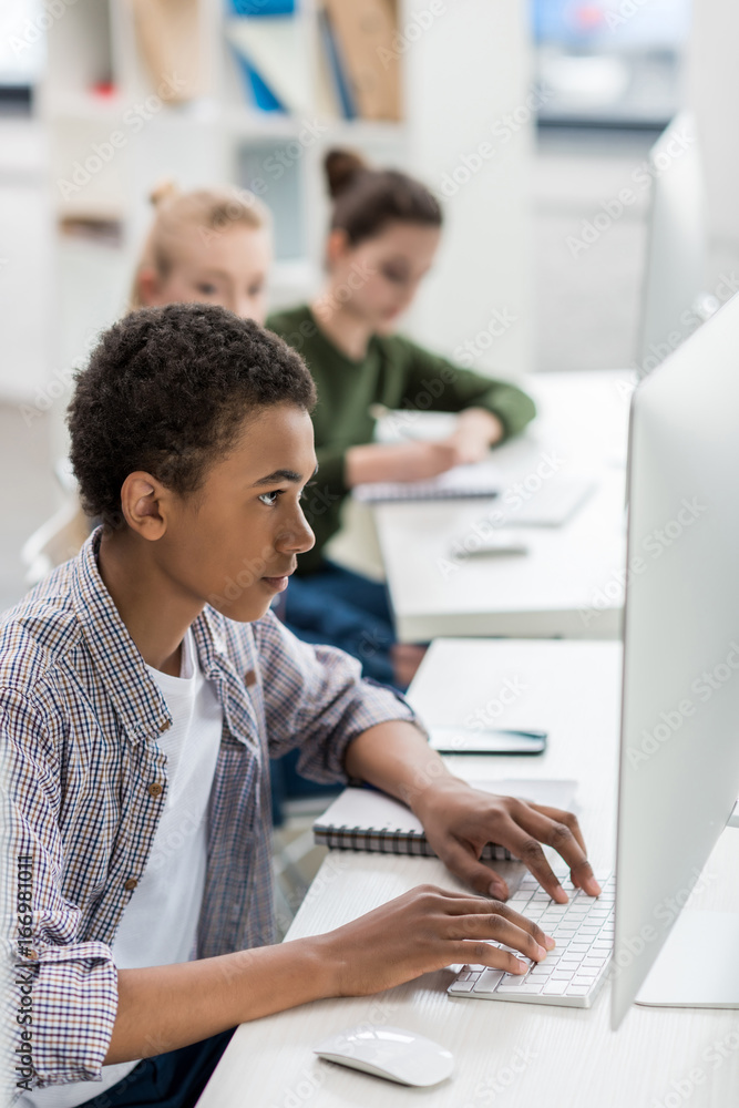 side view of african american teen boy typing on keyboard in front of ...