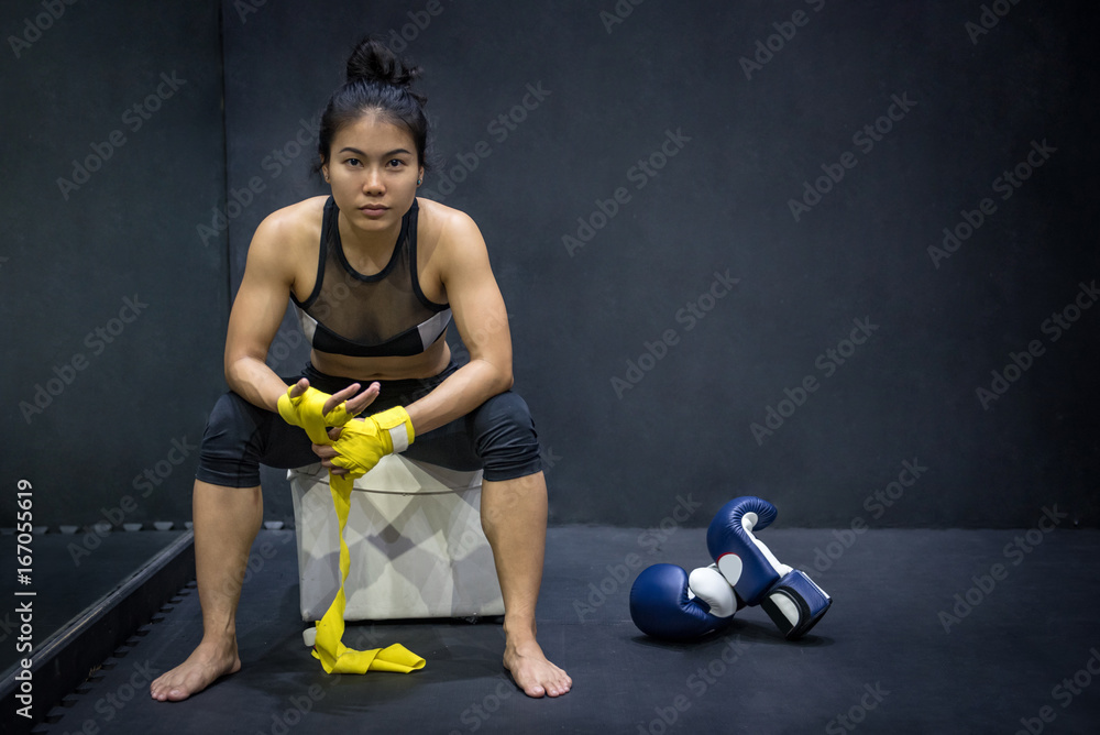 Asian female boxer wearing yellow strap on wrist sitting near boxing ...