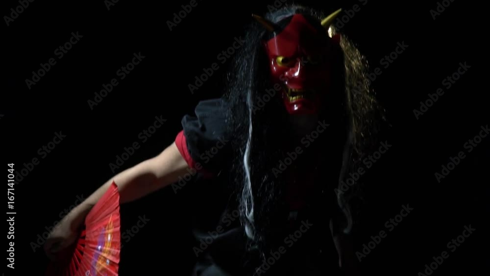 A freak in a mask of a Japanese demon with long hair come ous from ...