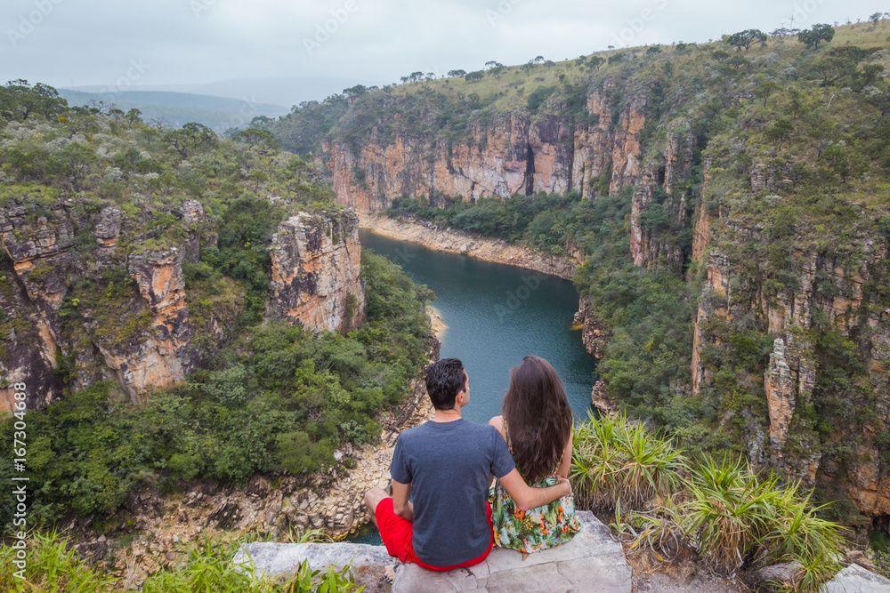 Couple on a rock overlooking a canyon with a river on the bottom and ...