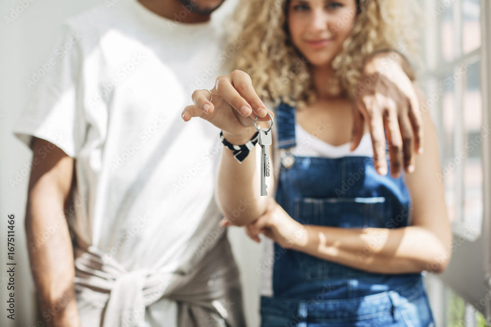 Portrait of woman holding keys standing with husband by window in house ...