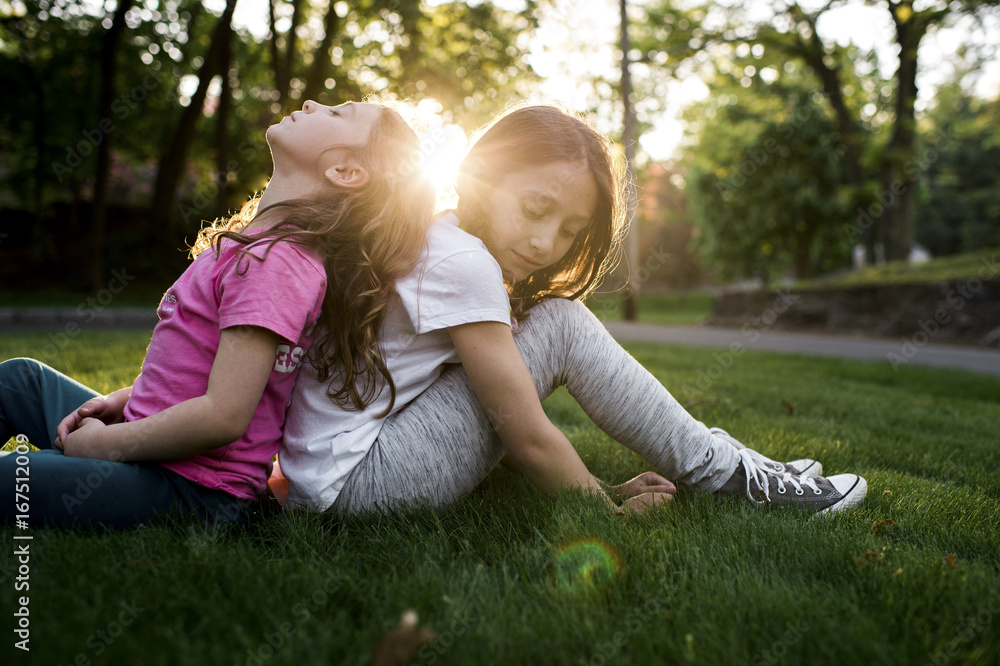Side view of sisters sitting back to back at park Stock Photo | Adobe Stock