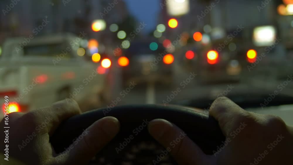 Driving a car through the city POV , hand on steering wheel close up ...