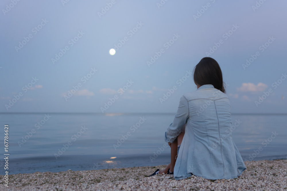 Young beautiful lonely girl is sitting on the beach and looking into ...