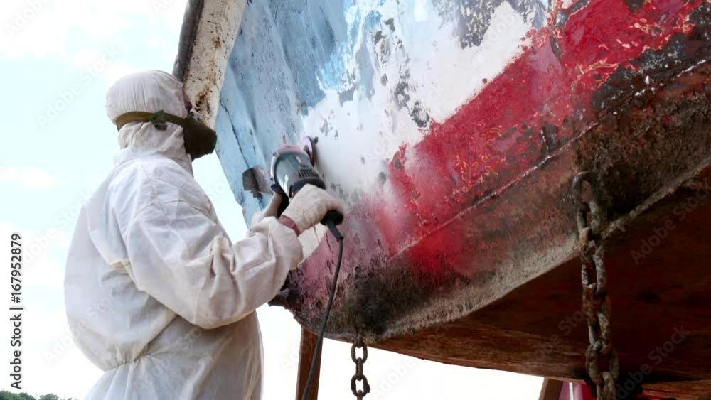 Working people tear off paint on metal in repairs process at shipyard ...