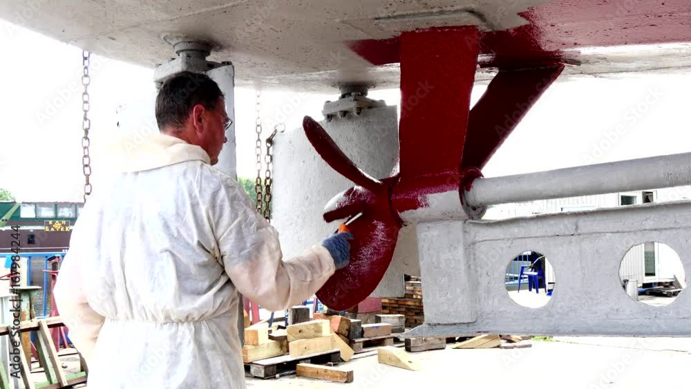 Worker paints metal of ship propeller red color at shipyard in port of ...