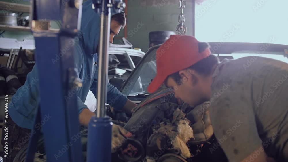 Two auto mechanics extract the motor from the hood of the car with the ...