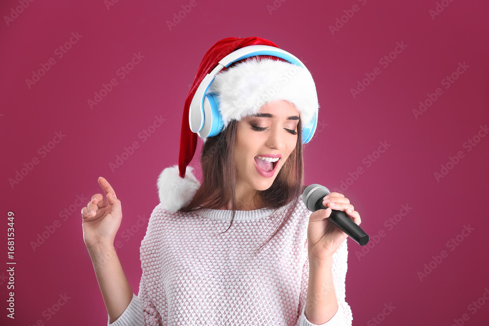 Beautiful young woman in Santa hat singing Christmas songs on color ...