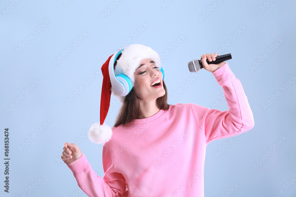 Beautiful young woman in Santa hat singing Christmas songs on color ...