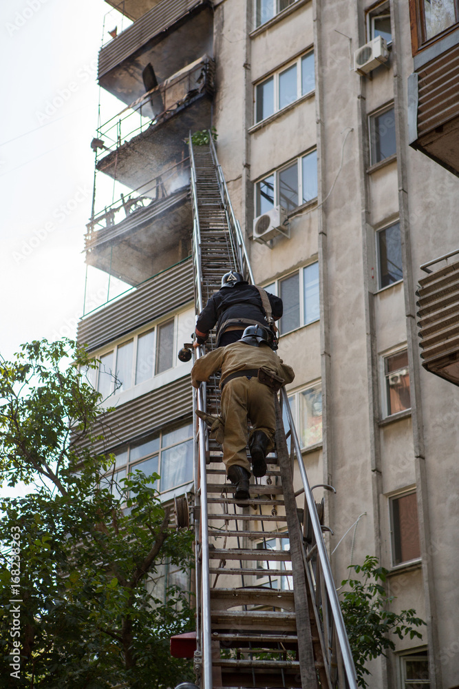 Firefighters climb the fire escape to extinguish fire on the upper ...