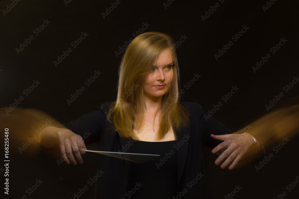 Young caucasian woman conductor gestures with baton and leaves light ...
