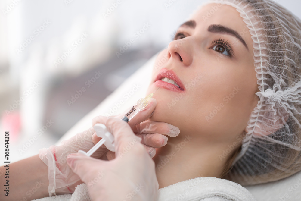 Hands of cosmetologist making injection in face, lips. Young woman gets ...