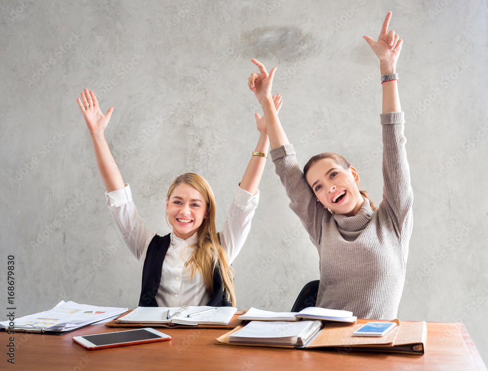 Two businesswoman smile and raise hands up, feeling happy on Friday ...