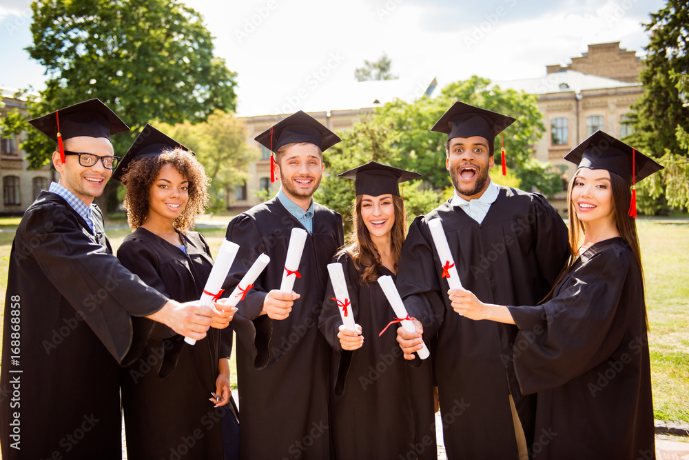 Six amazed successful attractive young graduates in black robes and ...