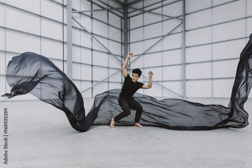 An asian male dancer in a warehouse bracing himself as silk fabric ...