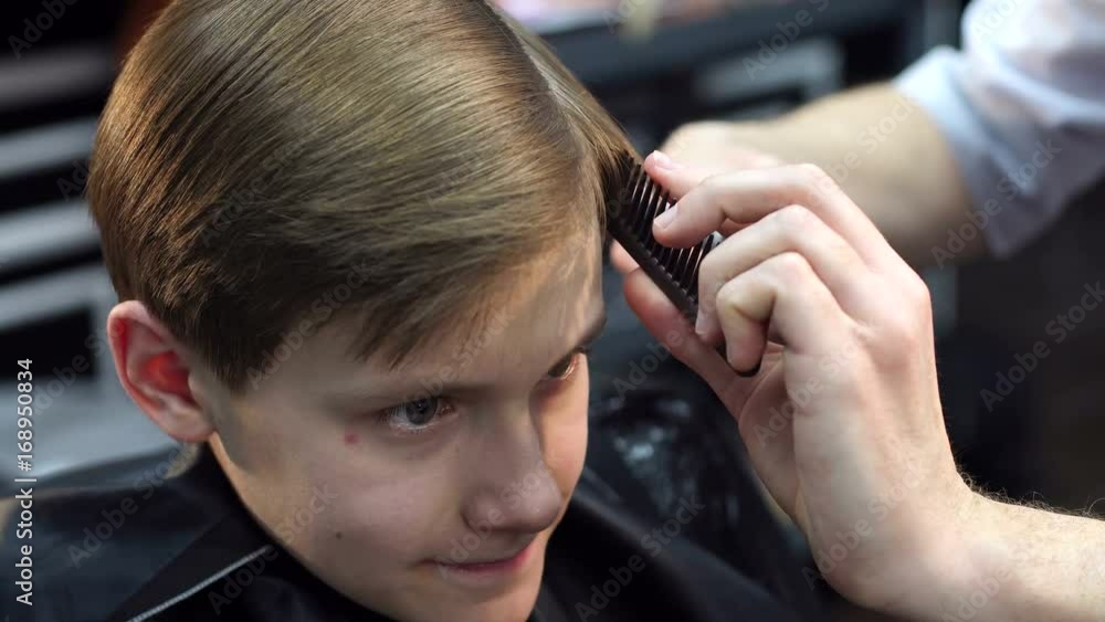 Portrait of a young teenage boy in the Barber shop. Barber cuts the ...