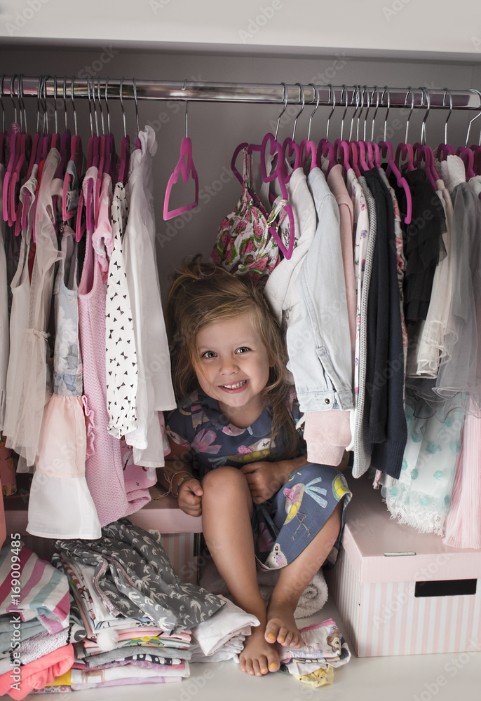 Beautiful little girl sitting in her wardrobe and smiling. Girl's ...