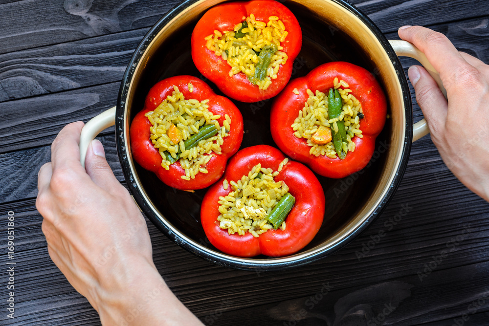 Chef holding a pan with four red stuffed peppers on dark rustic kitchen ...