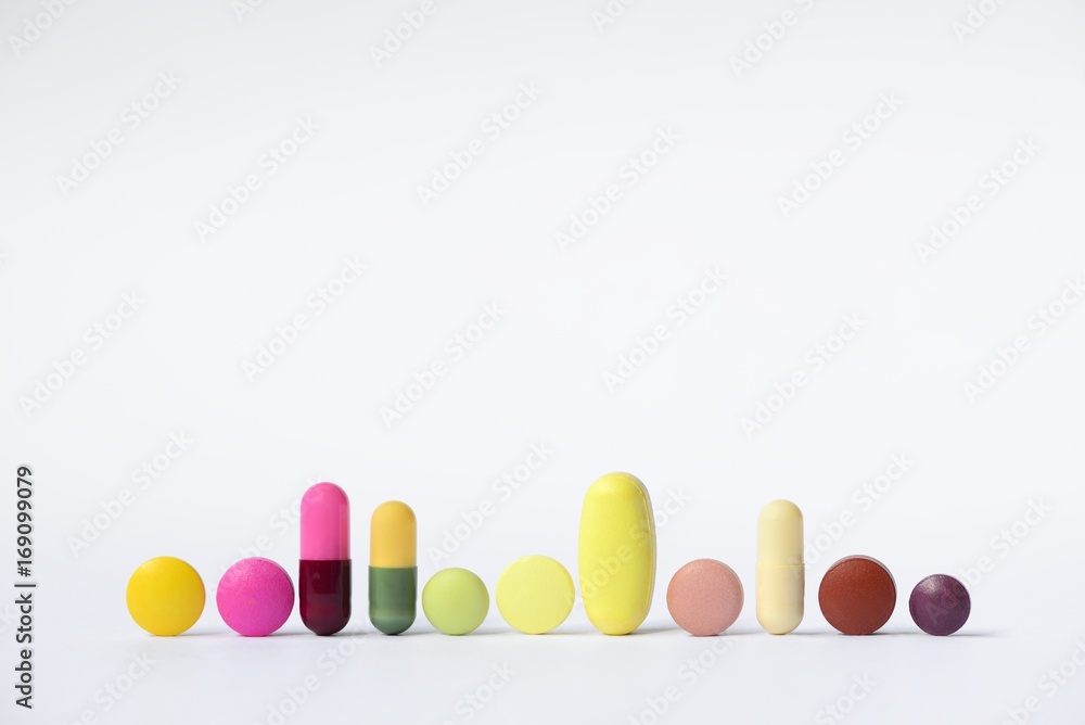 Colored tablets and capsules in a row, 11 pieces, white background ...