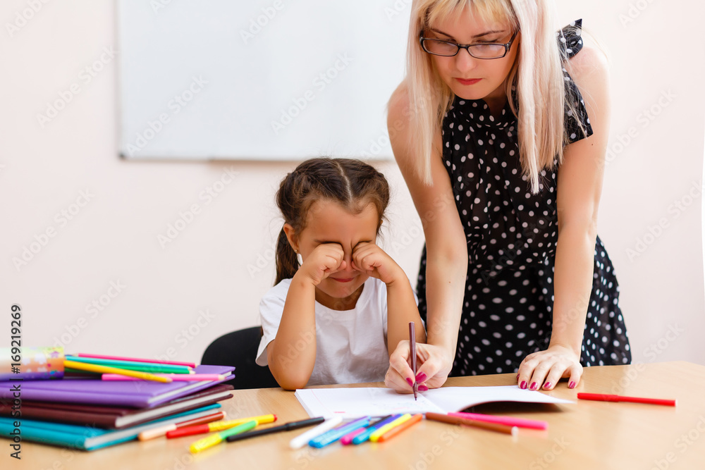 a strict teacher and a little student. Little girl is crying at a desk ...