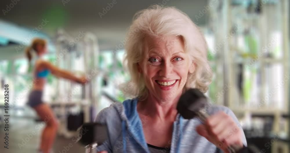 Mature woman in her 50s lifting dumbbells smiling at camera. Strong ...