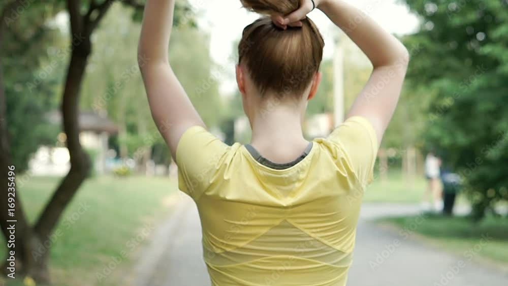 Girl standing back on the pathway and combing her hair into ponytail ...