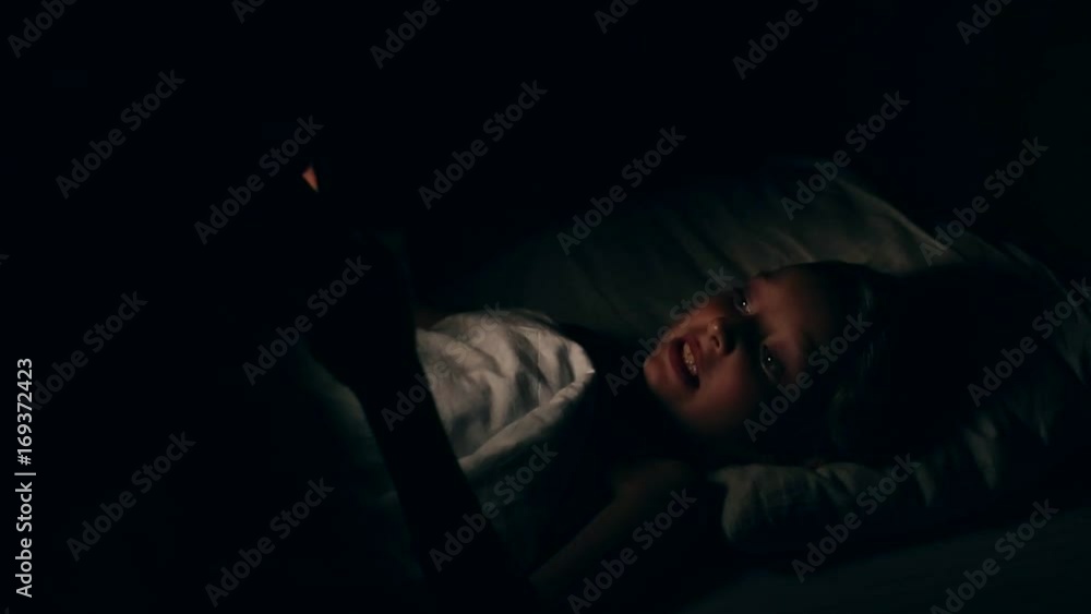 A girl lying in bed watching the horrors on the phone. Night movie viewing. The white girl does ...