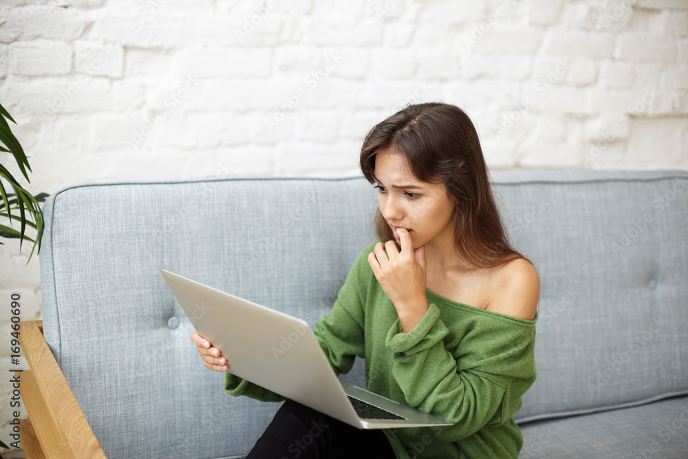 Cute young Latin female looking at screen of her generic notebook pc ...