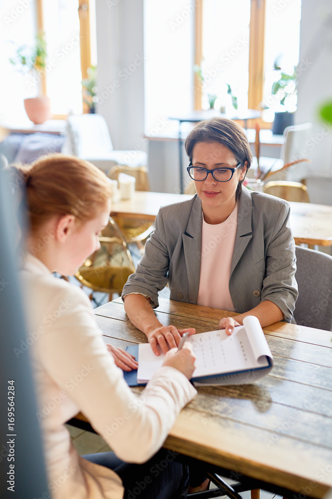 Young girl signing contract after interview with owner of cafe or ...