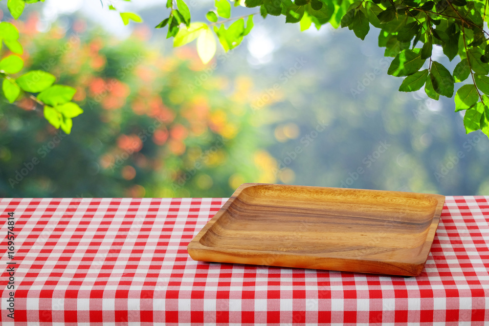 Empty wooden tray on table with red tablecloth over blur trees with ...