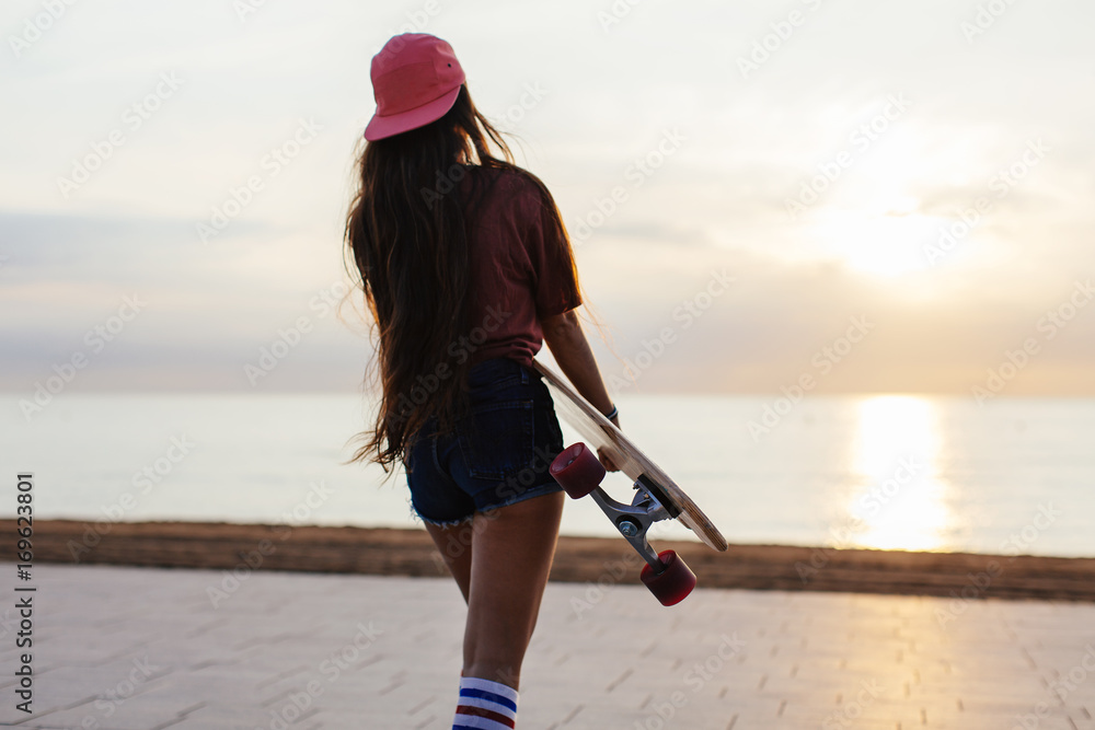 Girl holding her longboard walking by the beach at sunrise. Stock Photo ...