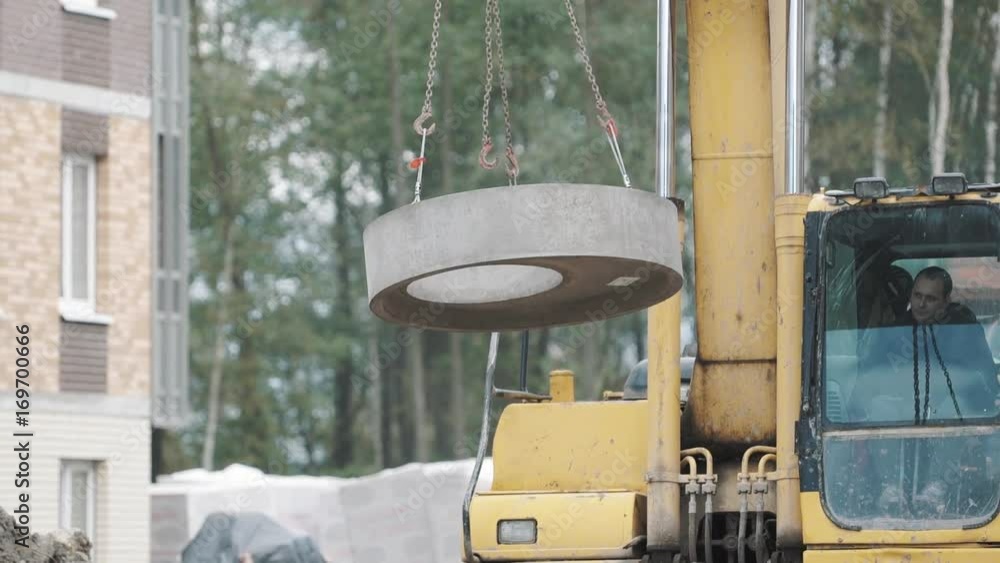Yellow excavator carries on chains concrete manhole ring at ...