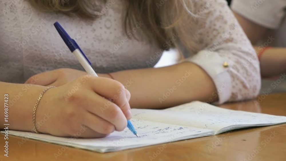 Student dressed in a white shirt sits at a school desk writing text in ...