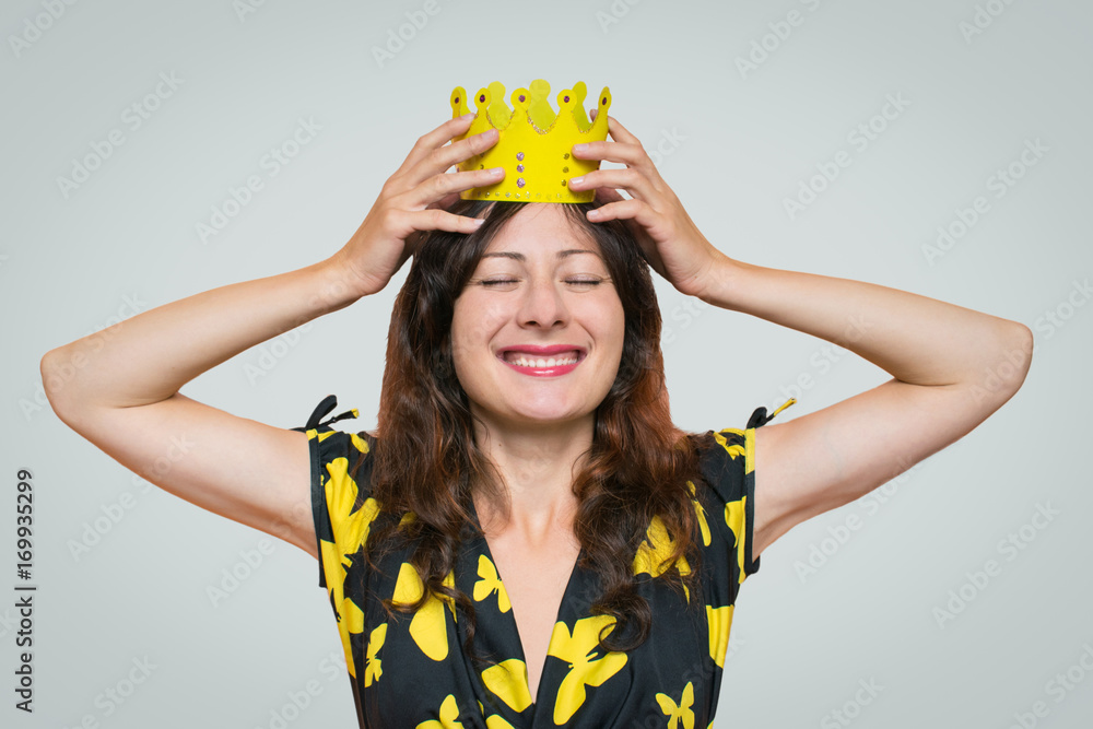 Beautiful young woman putting a paper crown on her head on the light ...