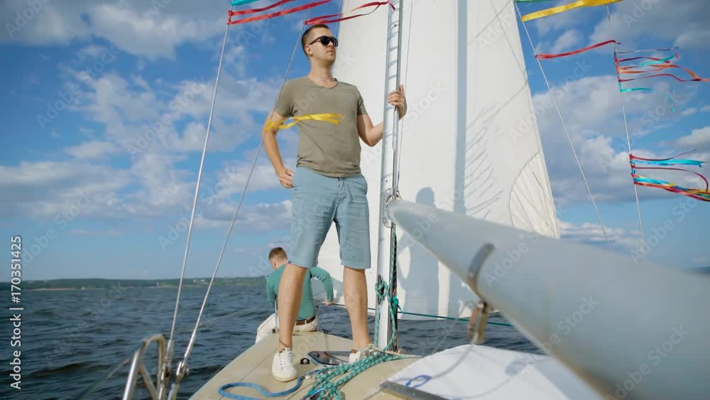 Handsome young man, who is the captait of this yacht, pulling on rope ...