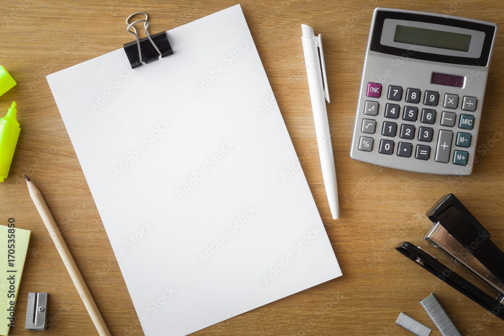 White paper with pen, pencil, calculator and stapler on the wooden ...
