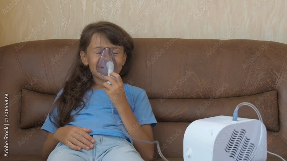A child does inhalations with a nebulizer. A beautiful little girl with ...