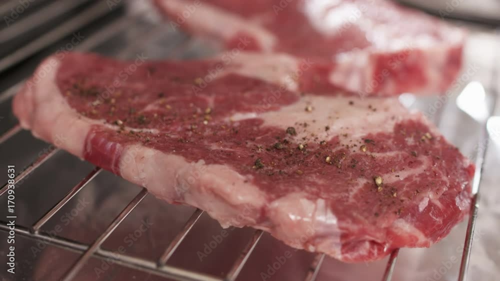 Two raw beef marbled steaks on cooling rack. Sprinkling fresh steaks ...